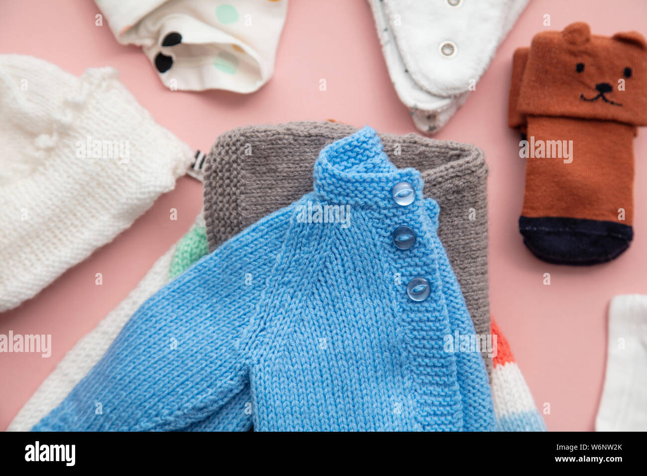 Cute handmade knitted baby clothes layout on a pastel pink background ...