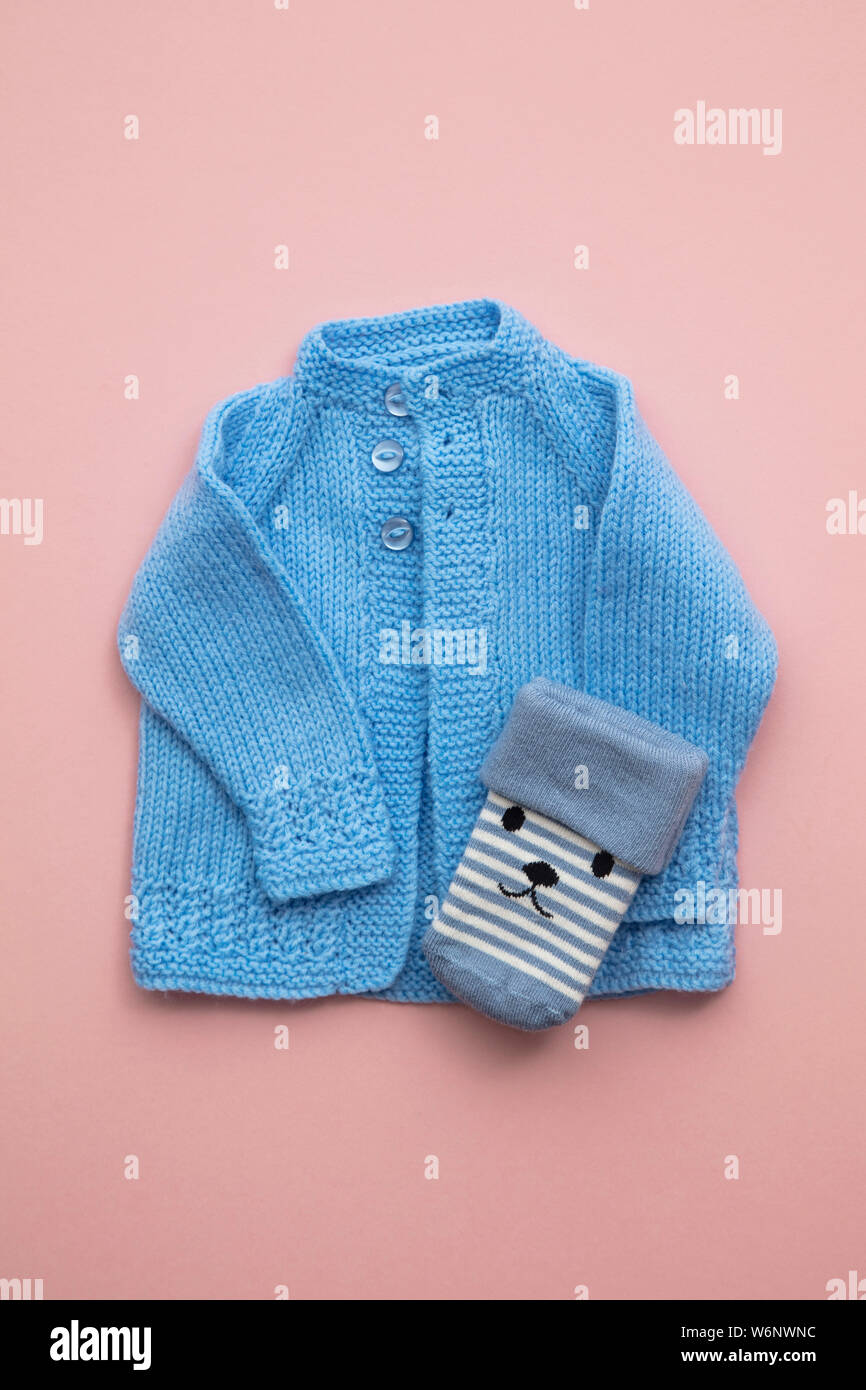 Cute handmade knitted baby clothes layout on a pastel pink background ...