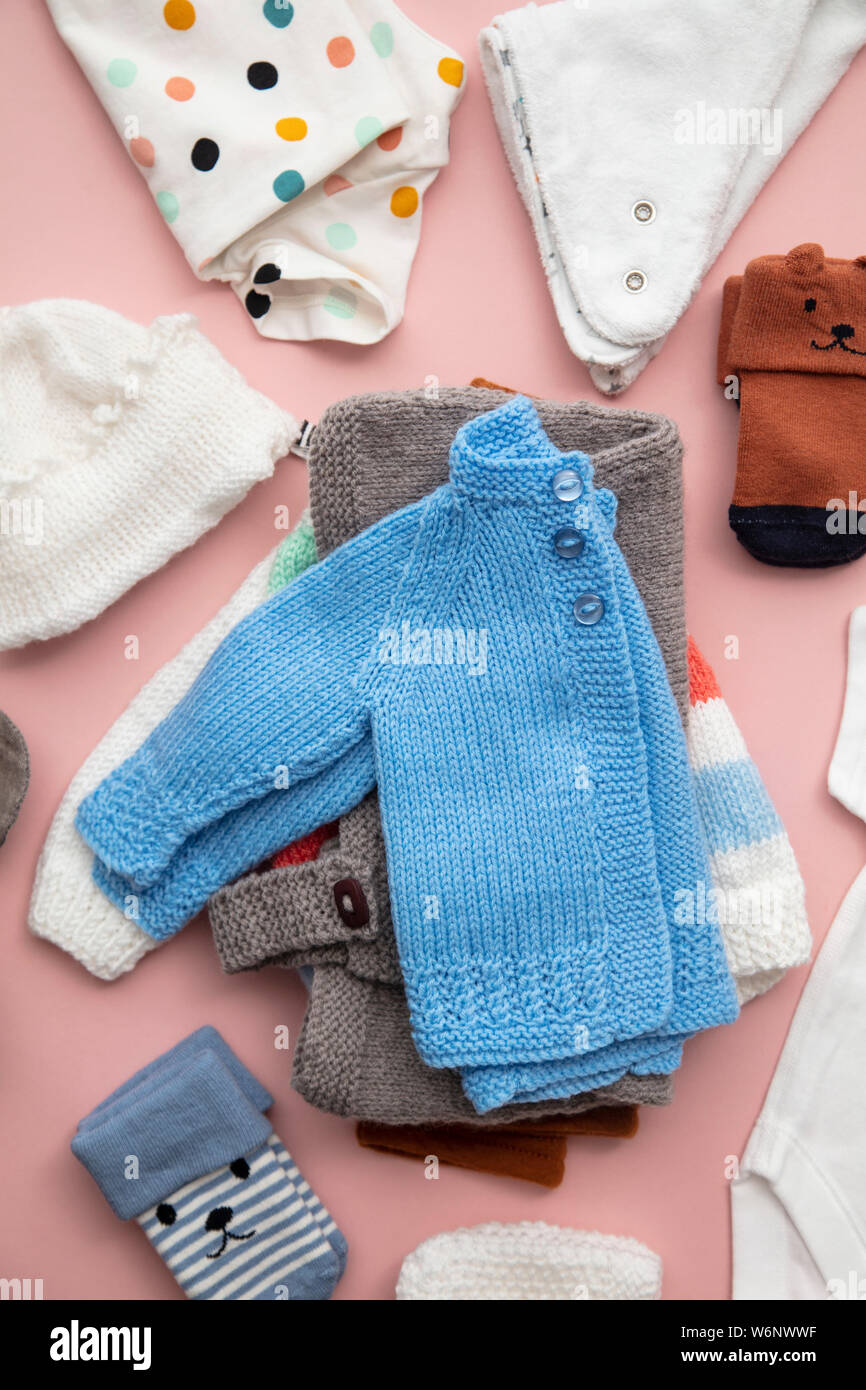 Cute handmade knitted baby clothes layout on a pastel pink background ...