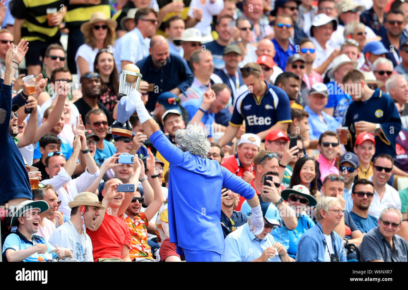 A cricket spectator in fancy dress lifts a mock world cup trophy during ...
