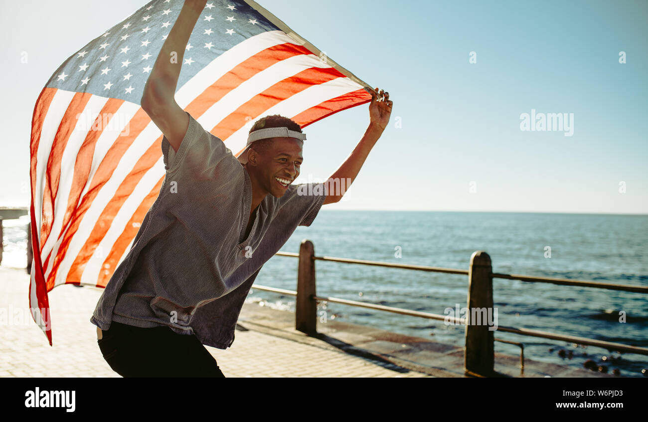 Smiling african man on seaside promenade with an american flag ...