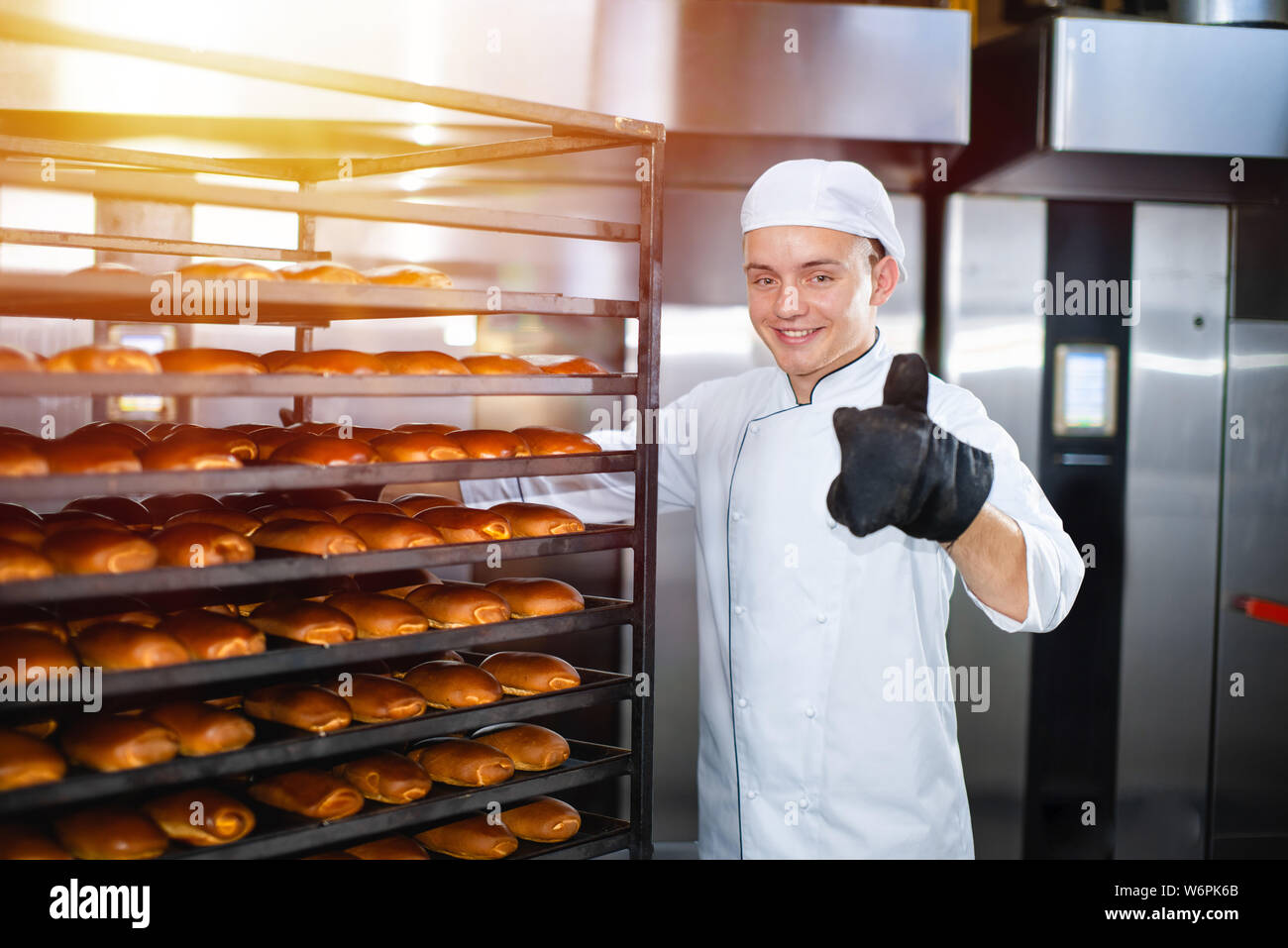 Baker with a hot baking trolley on a background of an industrial oven ...