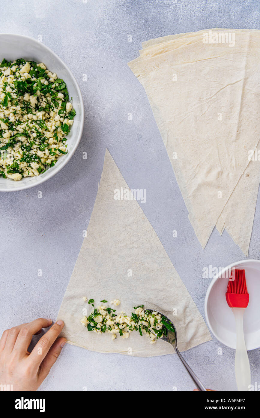 Woman filling triangle phyllo sheets with cheese and parsley mixture to ...