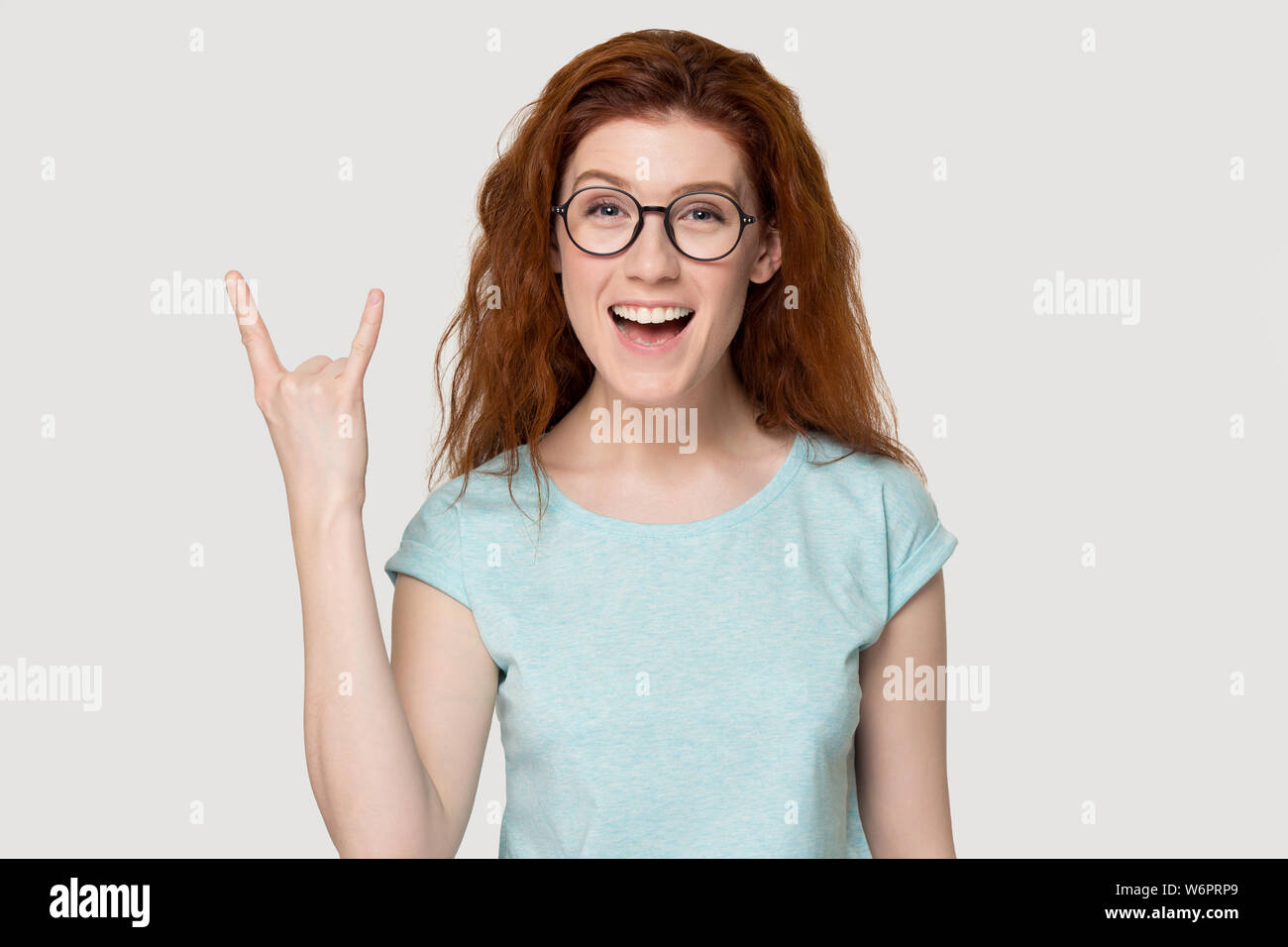 Cheerful redhead millennial woman showing rock and roll hand gesture ...