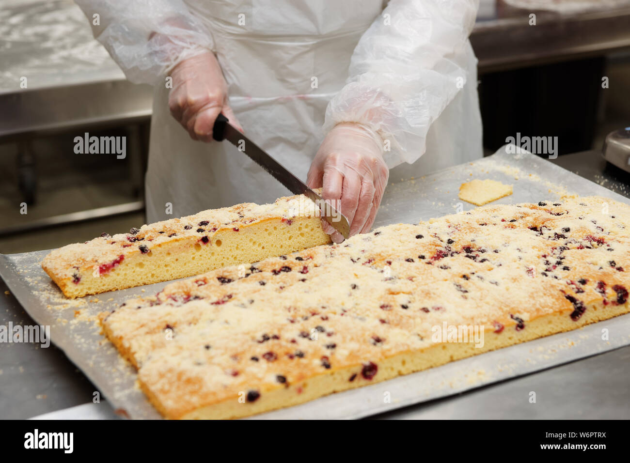 Female pastry chef chef is cutting biscuit in professional kitchen ...