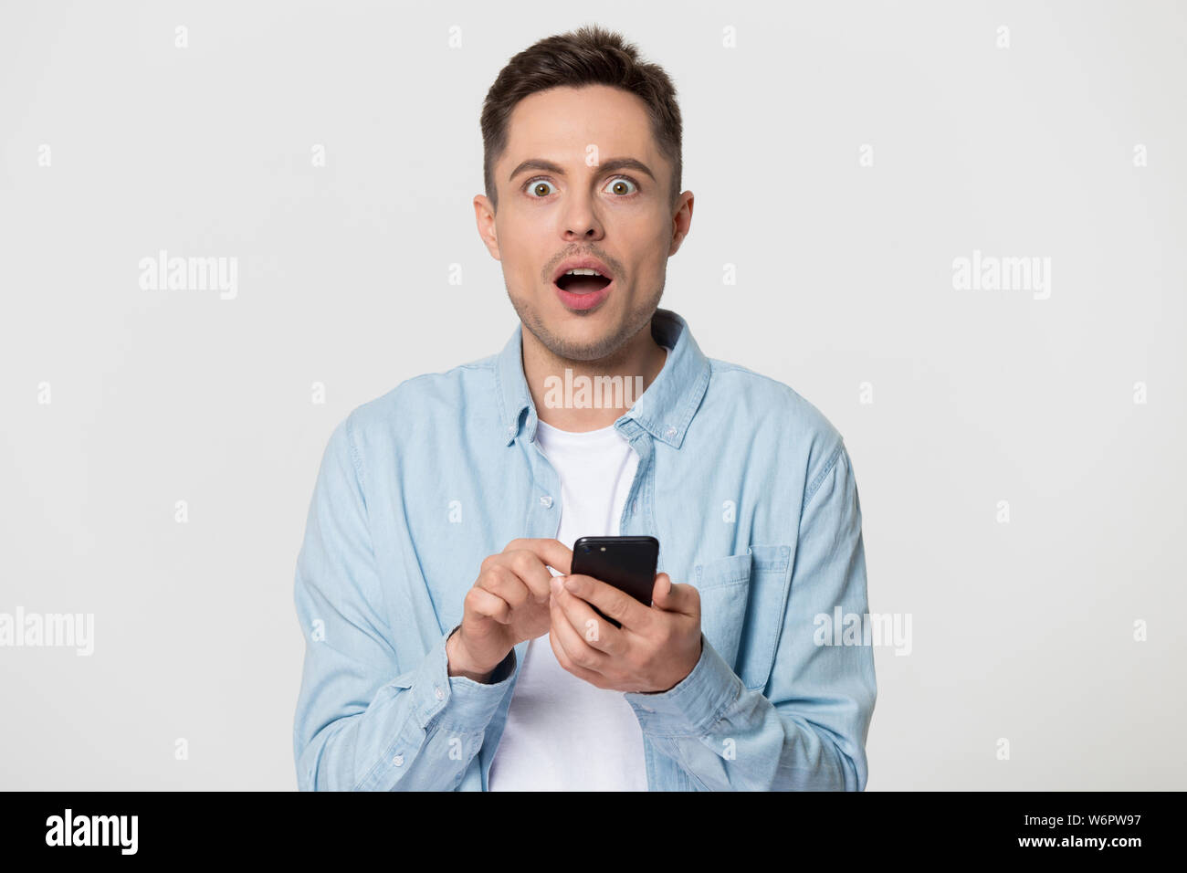 Shocked man holding phone astonished by online news pose indoors Stock ...