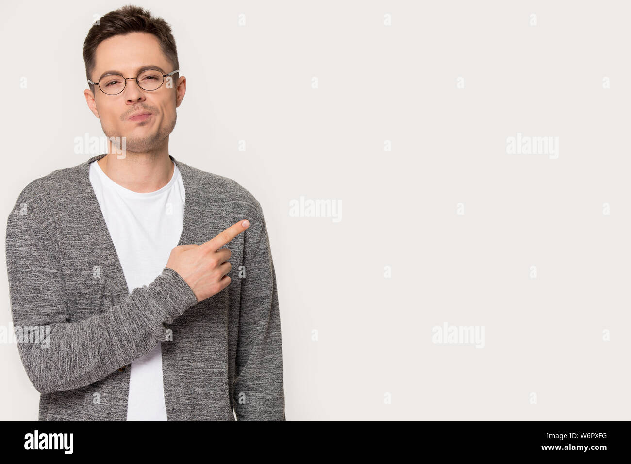 Sceptic guy pose on grey background pointing finger aside copyspace ...