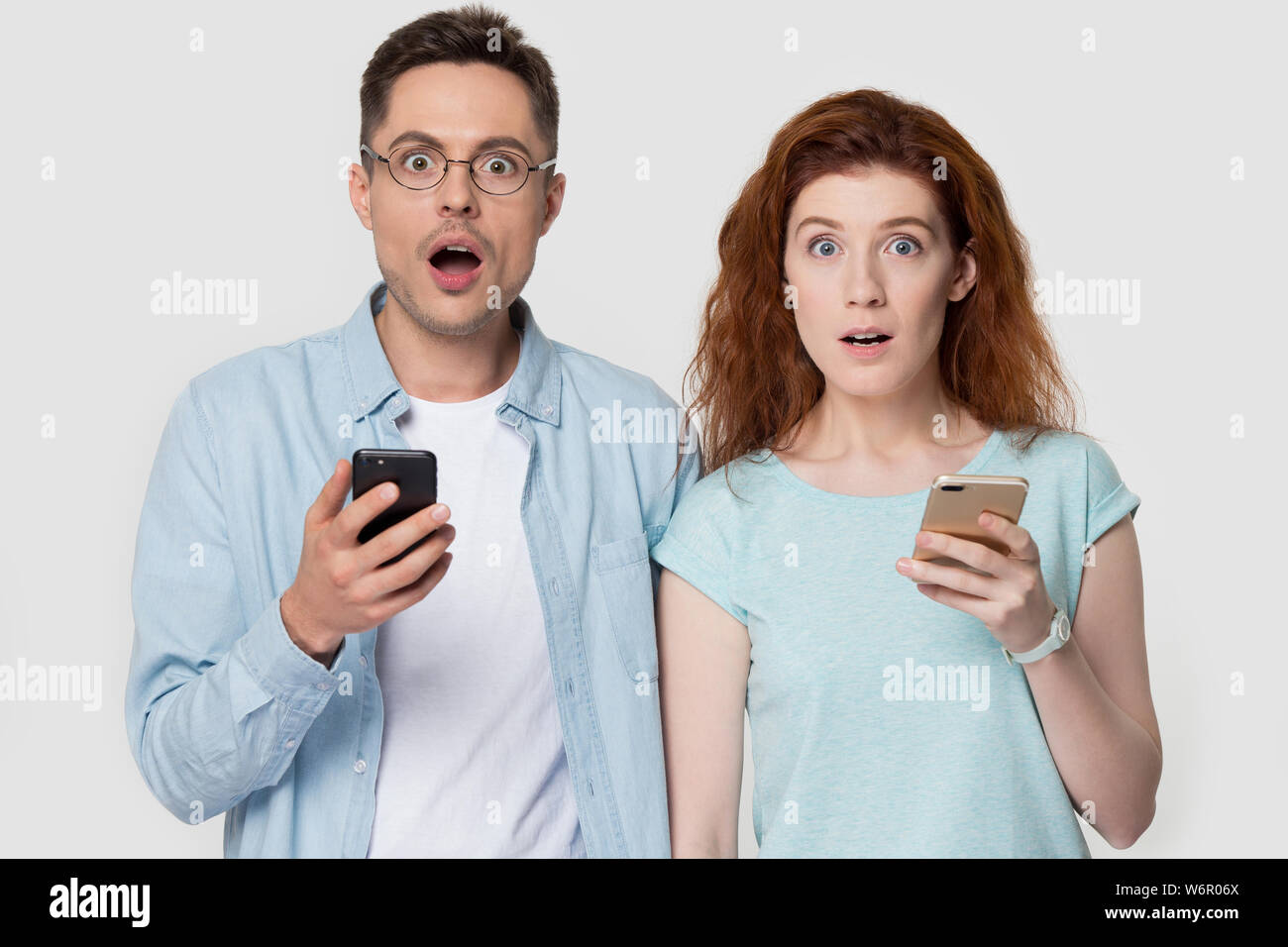 Shocked couple holds cell phones looking at camera pose indoors Stock ...