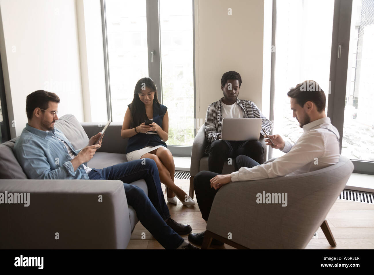 Multiethnic office workers using devices sitting in office room Stock ...