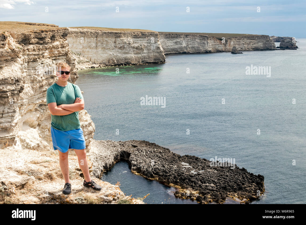 Young man on top of cliff in mountains and enjoying view of nature ...