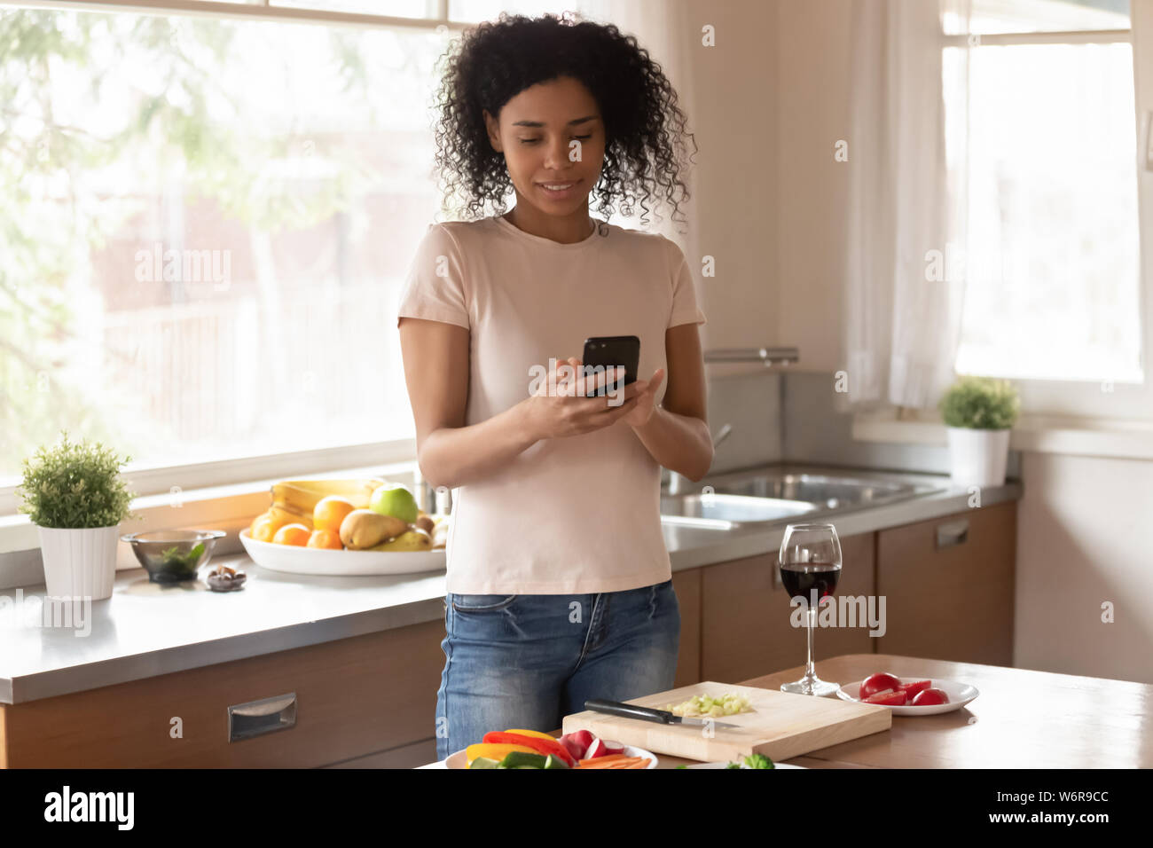 African woman standing in kitchen distracted from cooking using ...