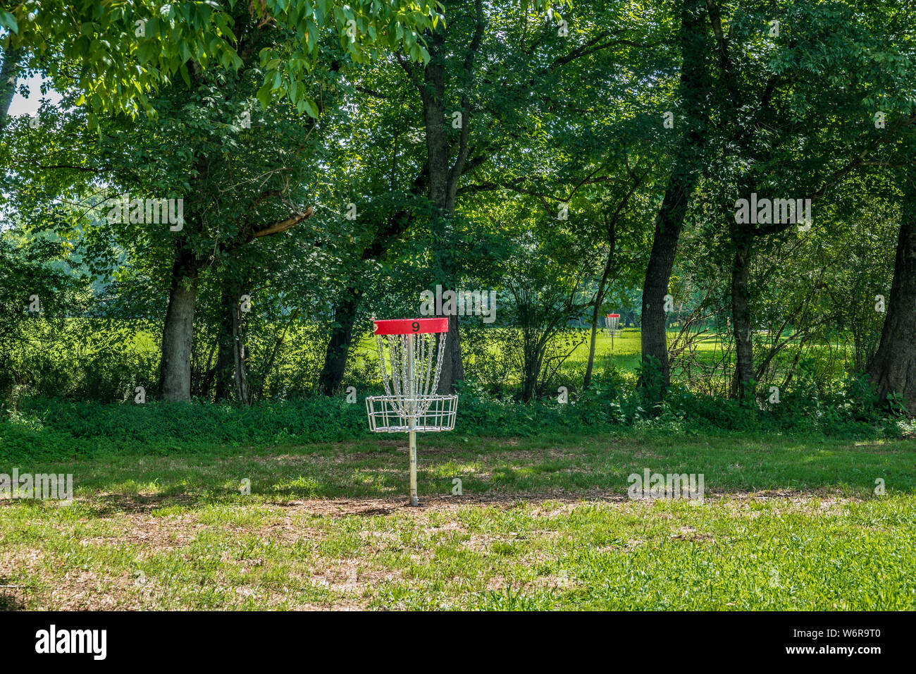 18-hole disc golf course with a metal disc basket alongside the woods ...