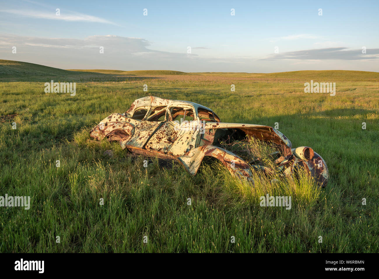 Wrecked and bullet-ridden old car on the open prairie in early morning ...