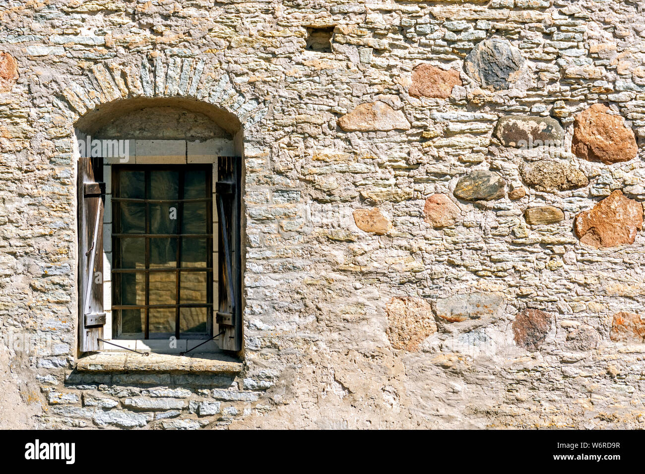 Window with arch, iron bars and wooden shutters on the fortress stone ...