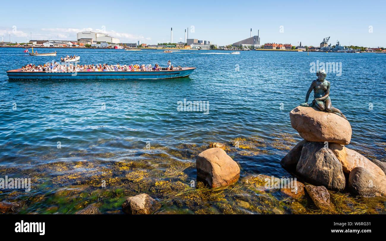 Iconic Little Mermaid statue with sightseeing canal boat in background in Copenhagen, denmark on ...