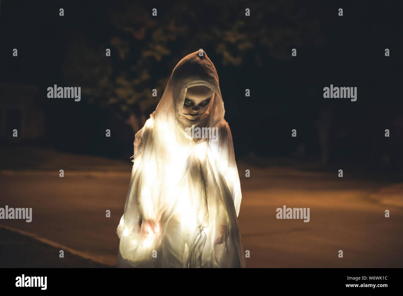 A child in a terrifying ghost costume stands near a street light on ...
