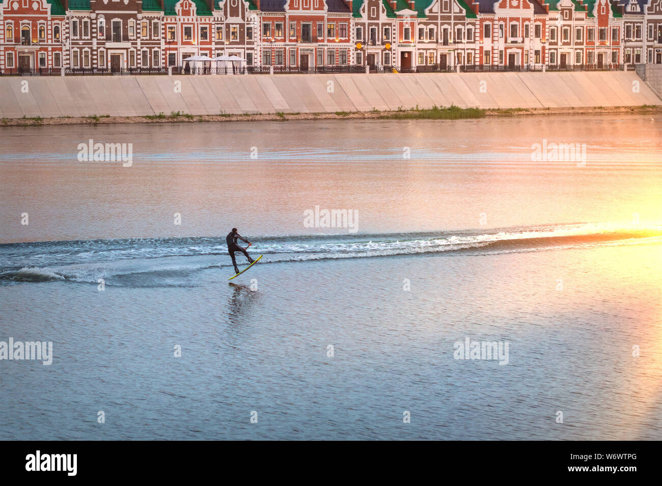 City wake surfer jumping on surface of river. Wakeboarder dressed in ...