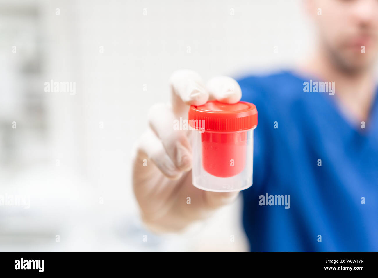 Doctor in blue uniform and medical gloves holding a container for semen ...