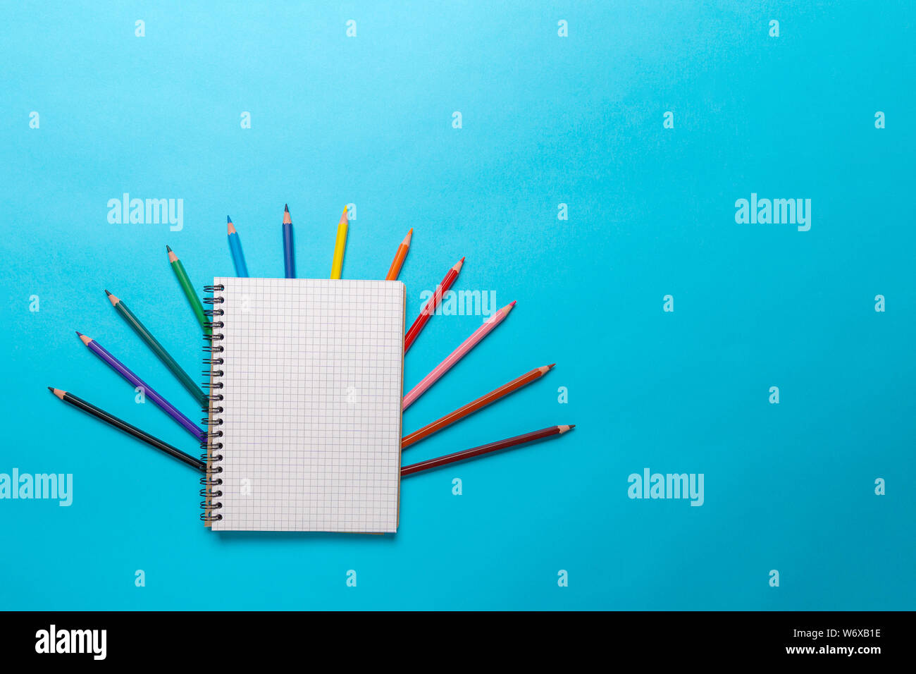 Color pencils and notepad on a blue background, soft focus. Blank for ...