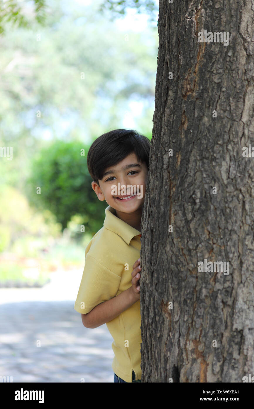 Boy peeking out from behind tree Stock Photo - Alamy