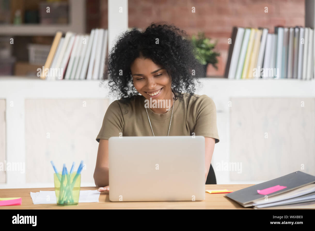 Front view african woman sitting at desk working on laptop Stock Photo ...