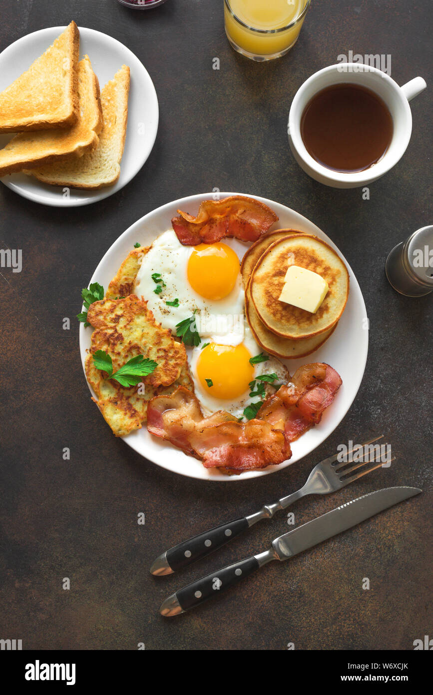 Full American Breakfast on dark, top view, copy space. Sunny side fried eggs, roasted bacon ...