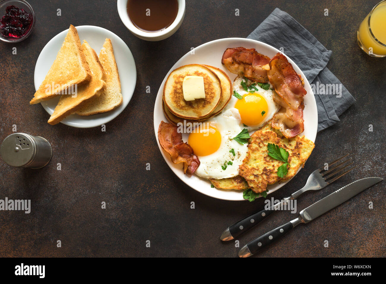 Full American Breakfast on dark, top view. Sunny side fried eggs, roasted bacon, hash brown ...