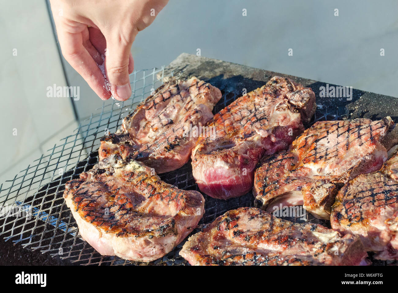 Cooks hand salt the meat in a barbecue. Grilling meat. Portioned steaks ...