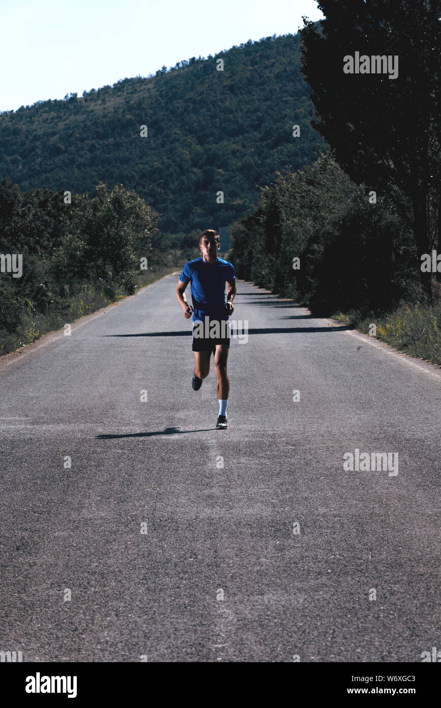 Male athlete running on an empty road in the woods while trying to get ...