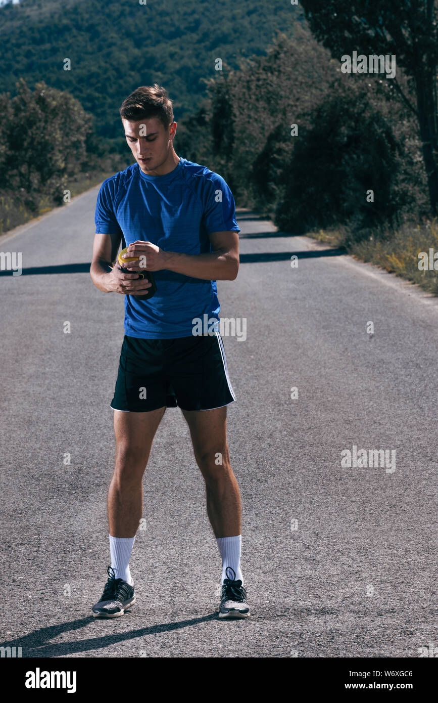 Fit male runner drinking water from a water bottle on an empty road in ...