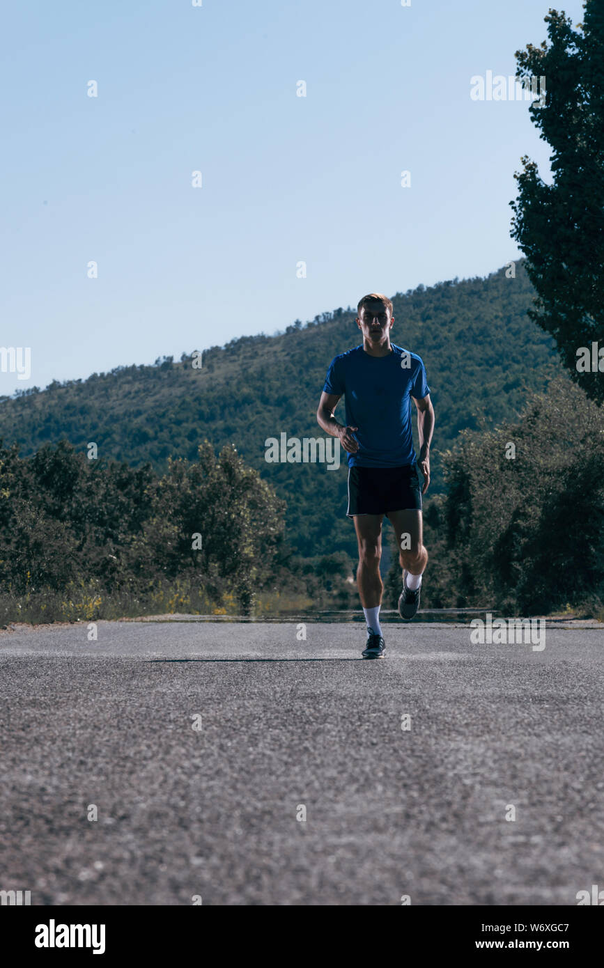 Male athlete running on an empty road in the woods while trying to get ...