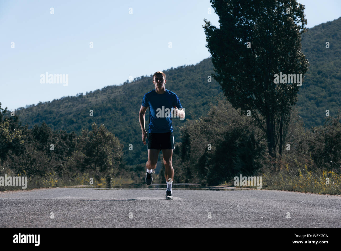 Male athlete running on an empty road in the woods while trying to get ...