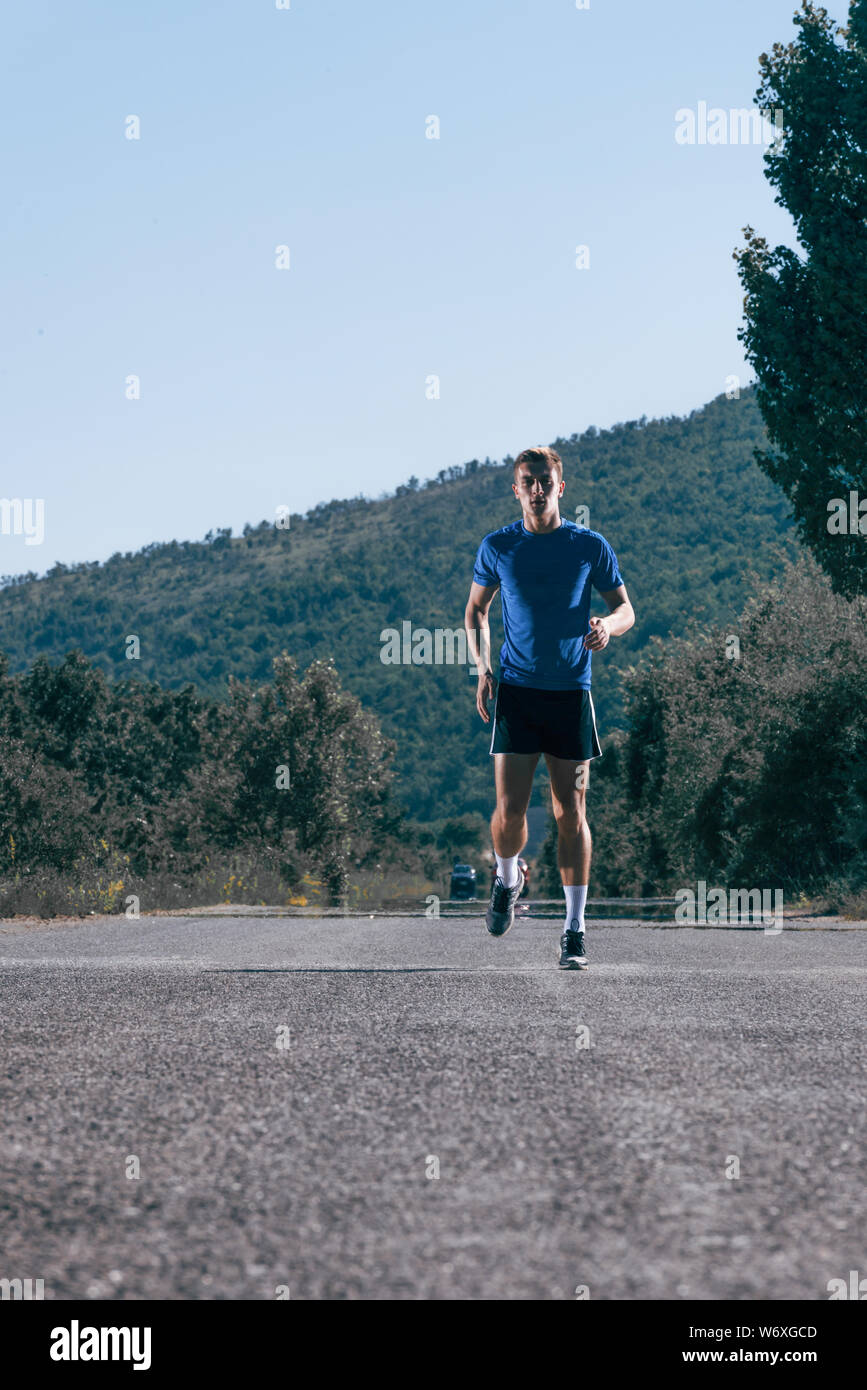 Male athlete running on an empty road in the woods while trying to get ...