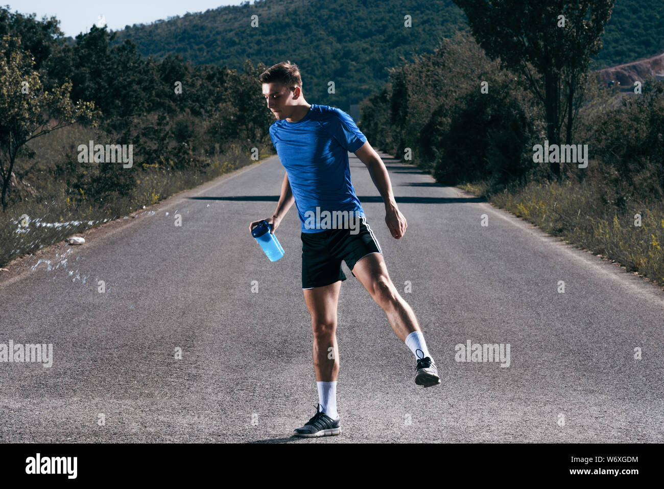 Fit male runner drinking water from a water bottle on an empty road in ...