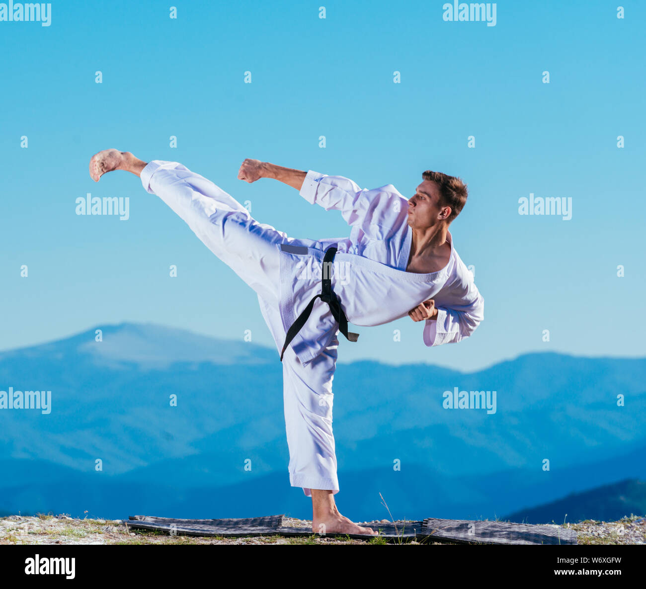 Karate man in a kimono performs a side leg-foot kick(Mae-geri) while ...