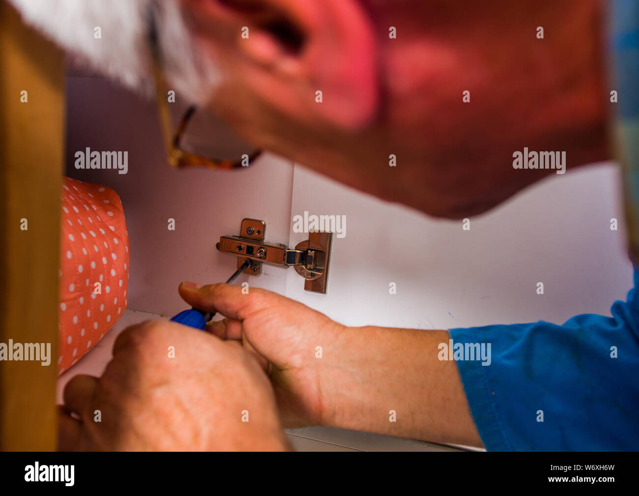 Serious handyman is standing in the kitchen and fixing the cupboard ...