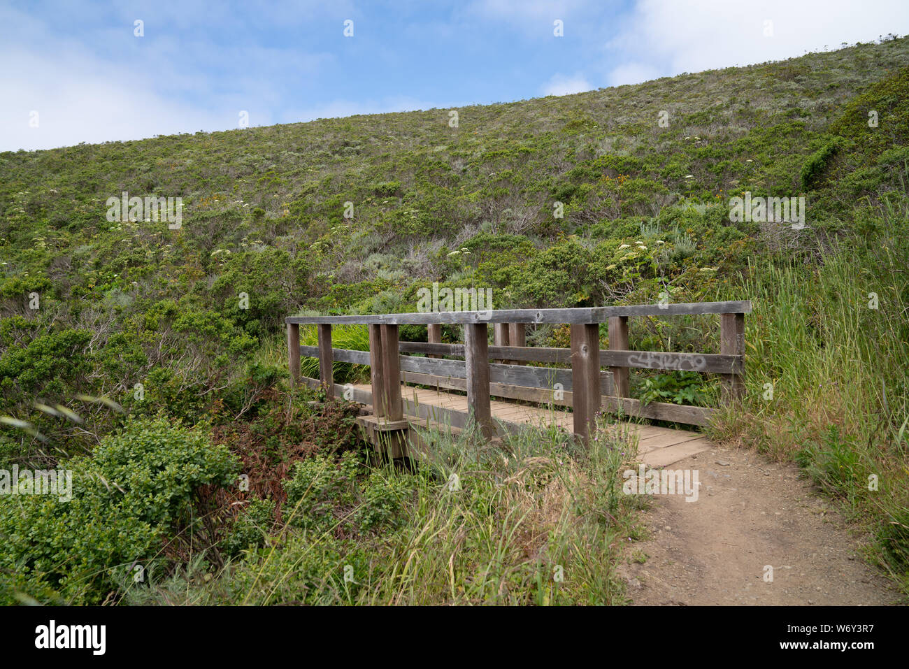 Small wooden bridge on dirt trail path below large hill Stock Photo - Alamy