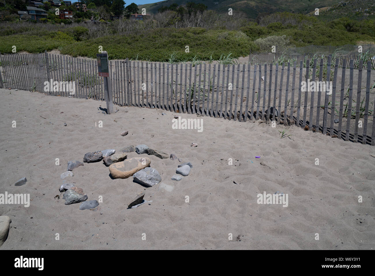 Beach designated bonfire area near fence, hills, and warning sign Stock ...