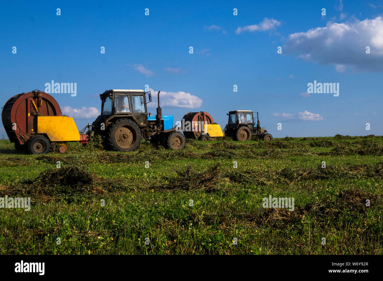 Agricultural machinery, a tractor collecting grass in a field against a ...