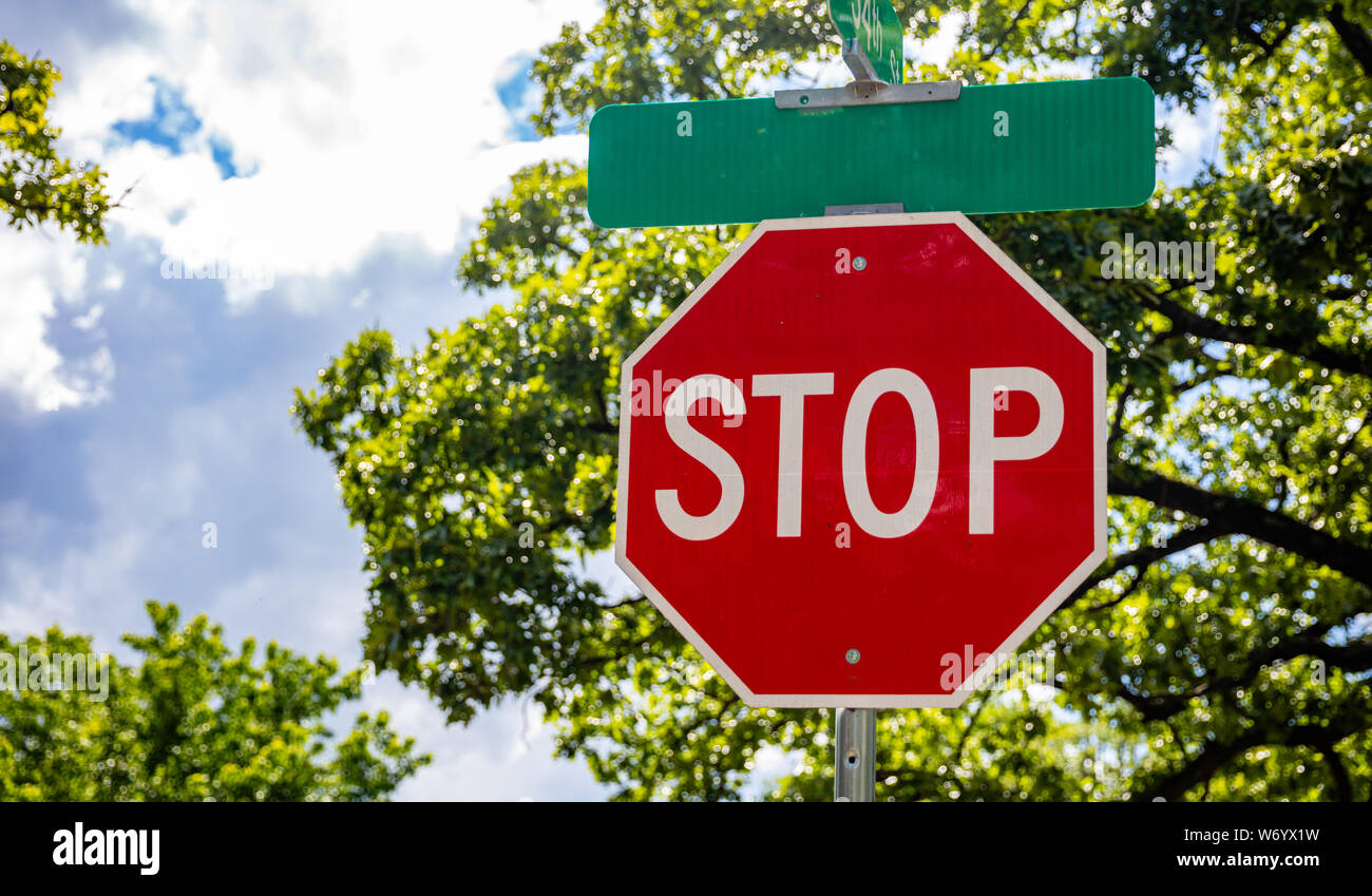 Stop road sign on an intersection. Blur trees and blue sky background ...