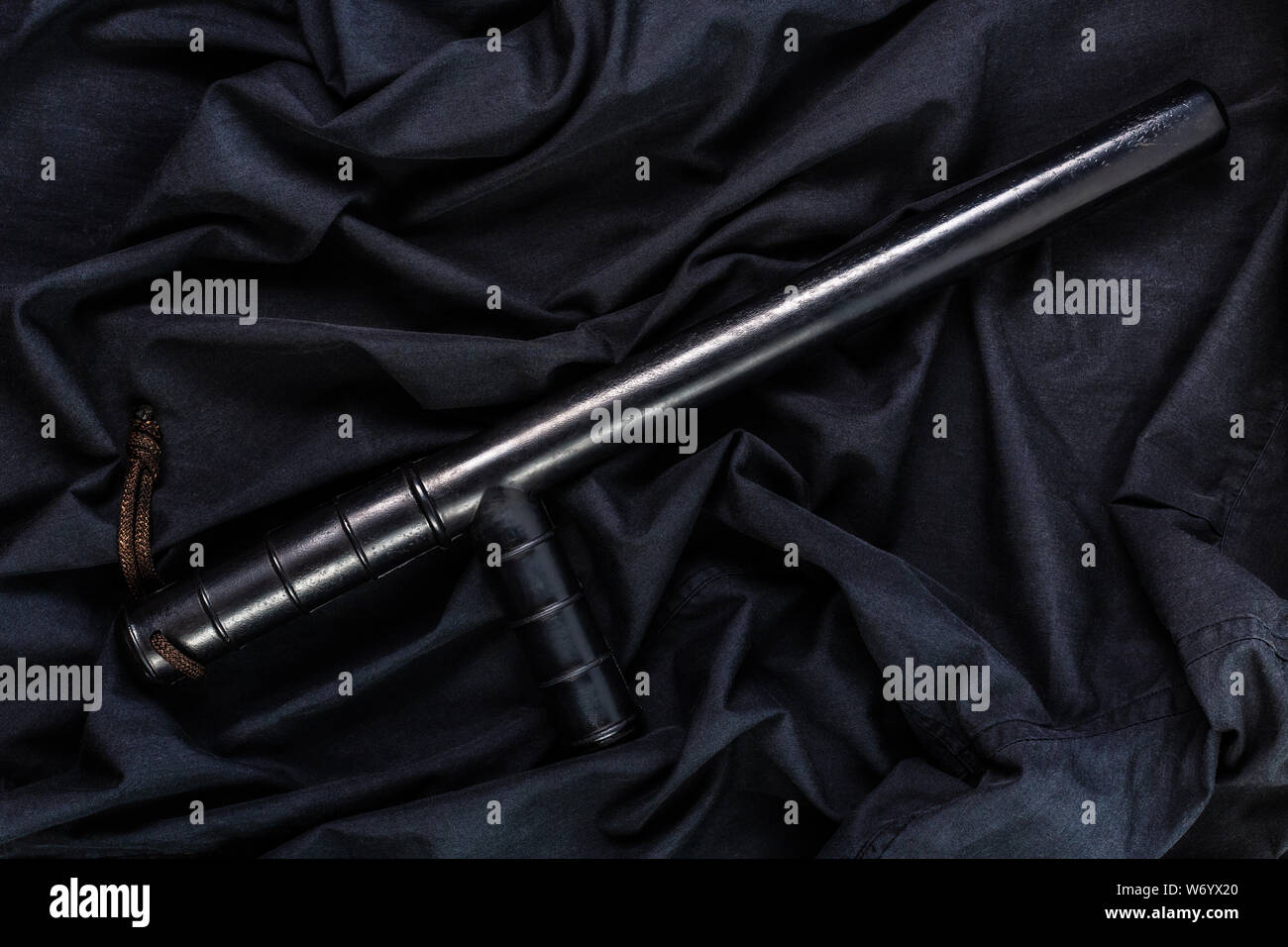 black rubber police baton on black shirt wrinkled cloth low-key flat ...