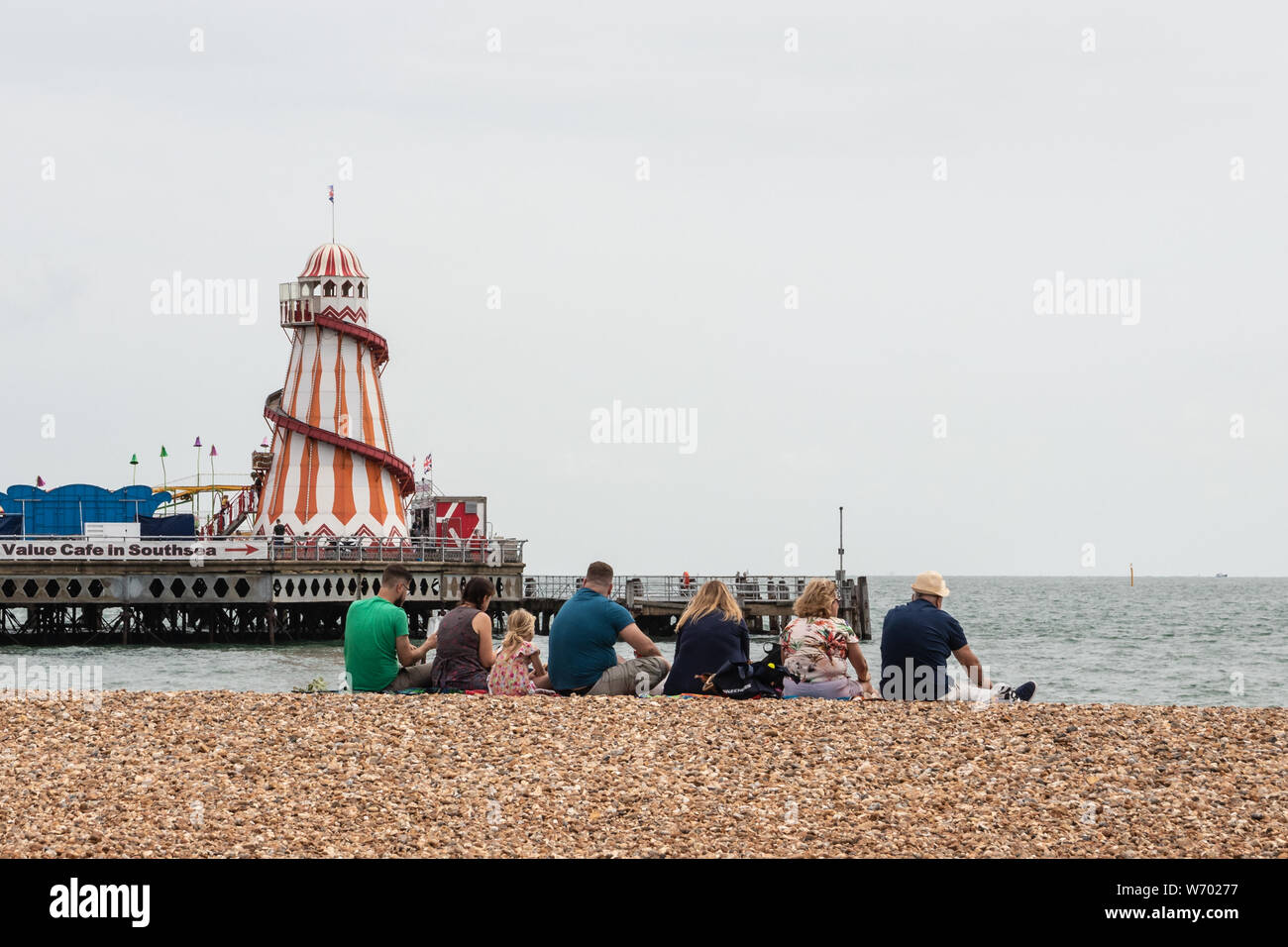A family sat on the pebble beach at Southsea with south parade pier and ...
