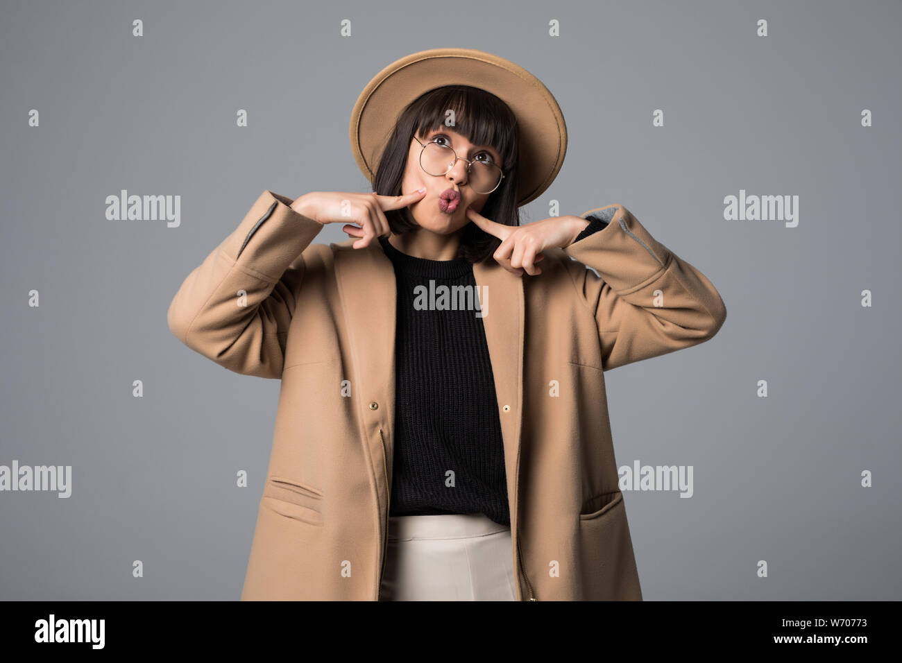 Young woman pointed on cheeks wear in beige coat and hat isolated on ...