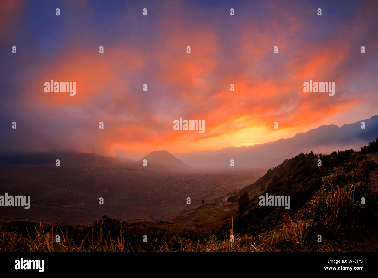 Orange sky glowing at sunset above erupting volcano Mount Bromo one of ...