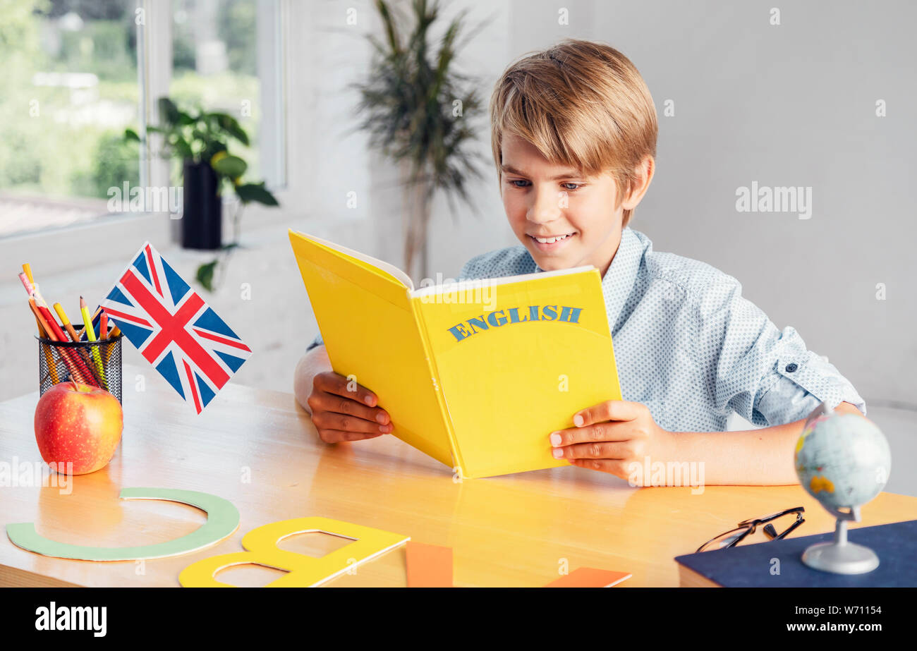 Happy smiling boy reading yellow english language book in light ...