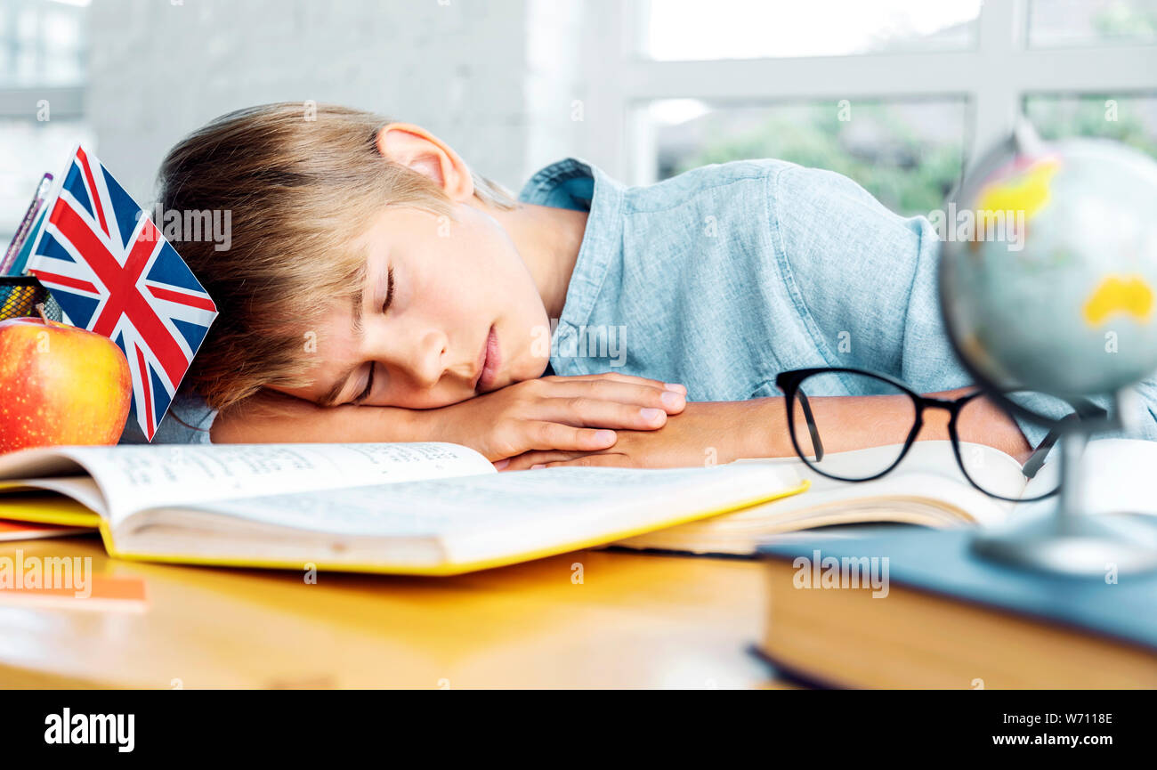 Bored young schoolboy napping in the classroom, table with textbooks ...