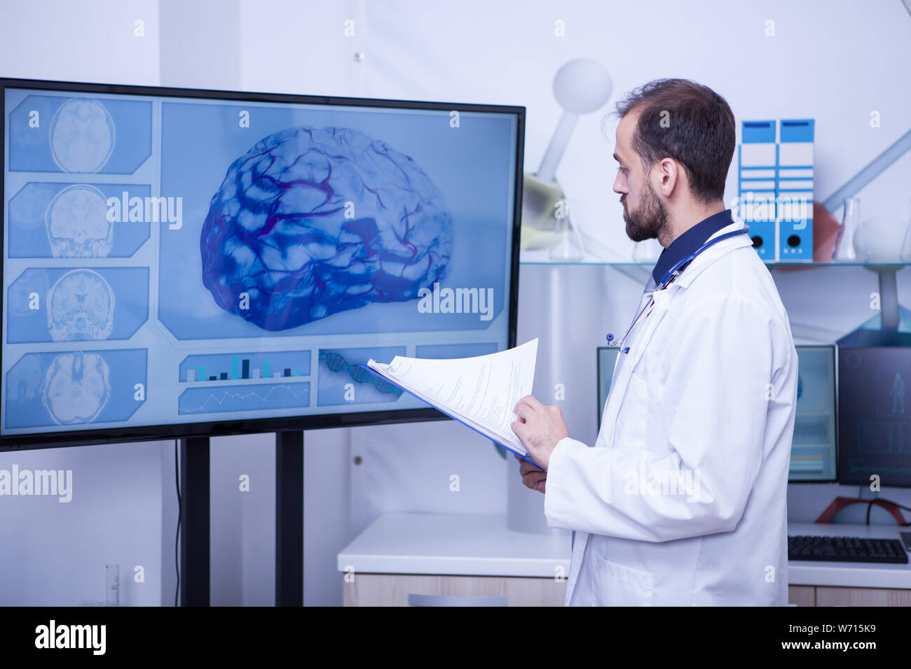 Doctor with clipboard on his hand looking at a brain on a big monitor ...