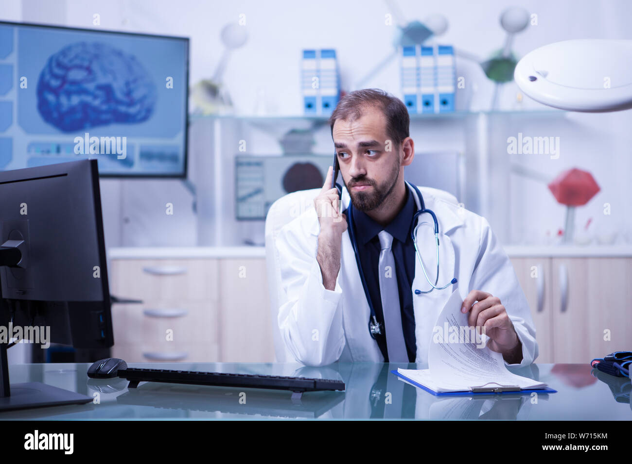 Male doctor using telephone while looking into his monitor from the ...
