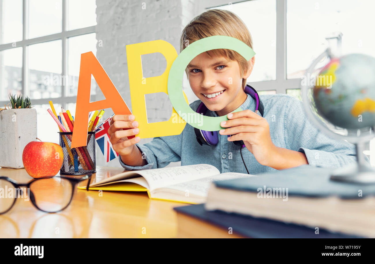 Handsome young boy holding colorful english letters while sitting in ...