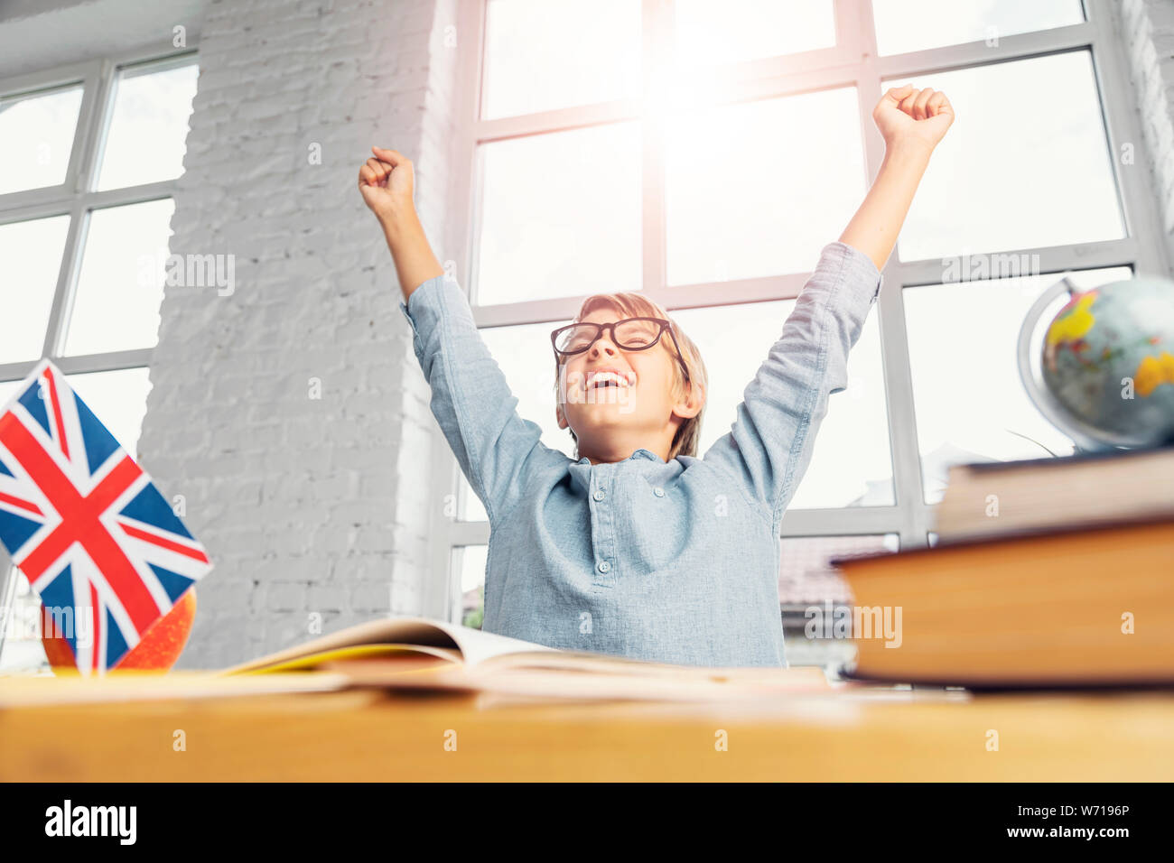 Happy successful schoolboy raises hands up in wide classroom ...